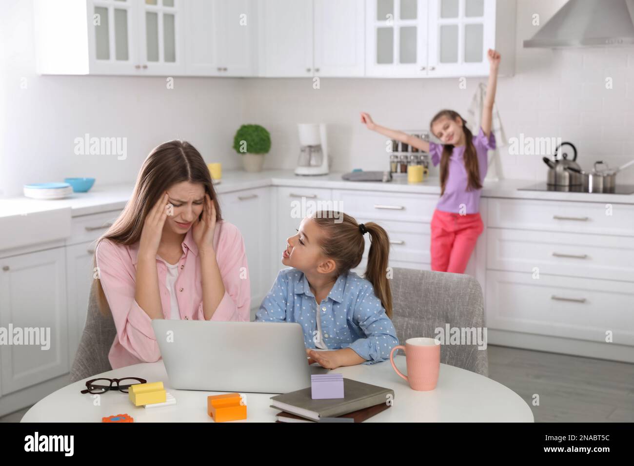 Children disturbing stressed woman in kitchen. Working from home during ...
