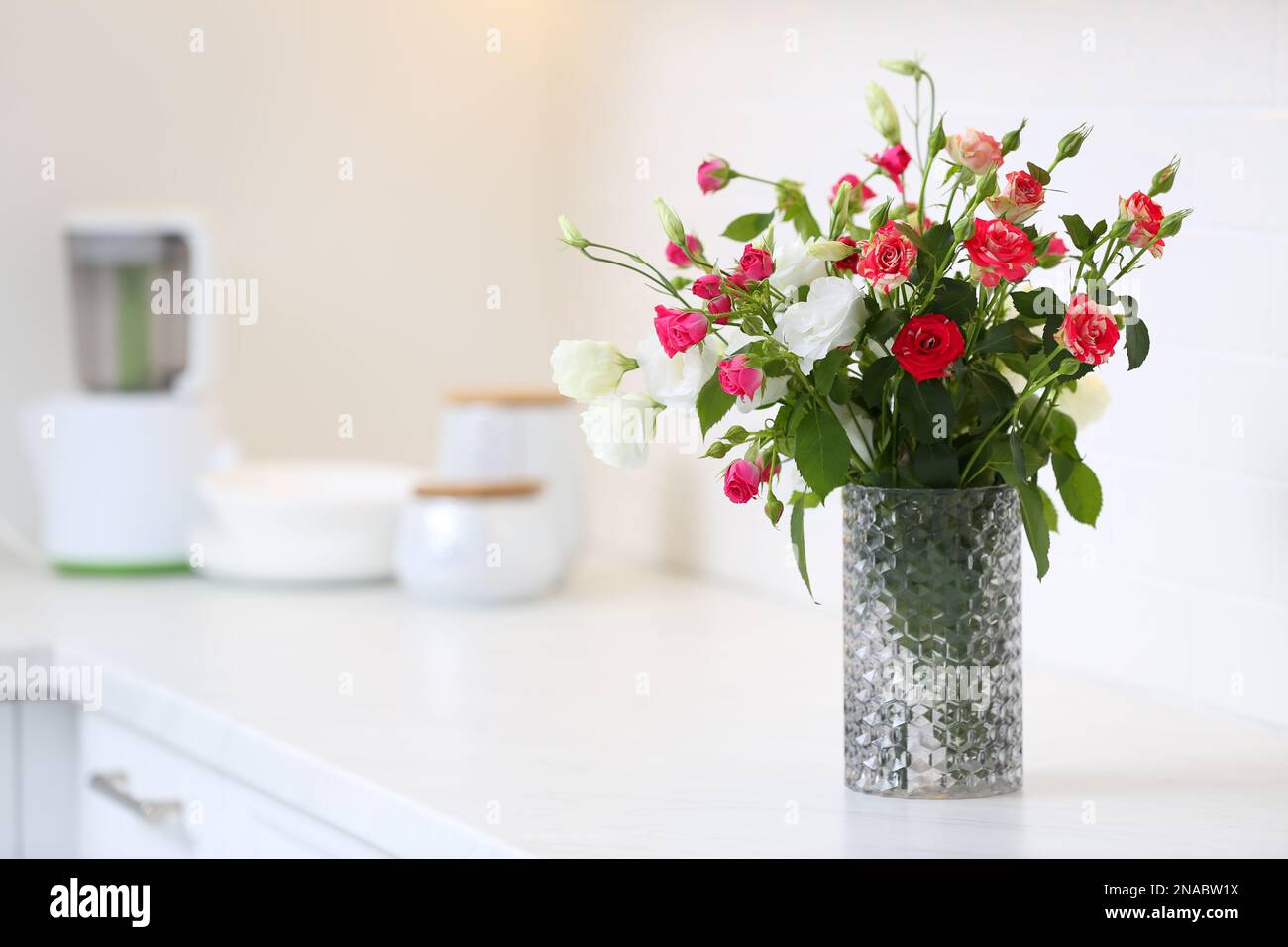Vase with beautiful flowers on white countertop in kitchen, space for ...