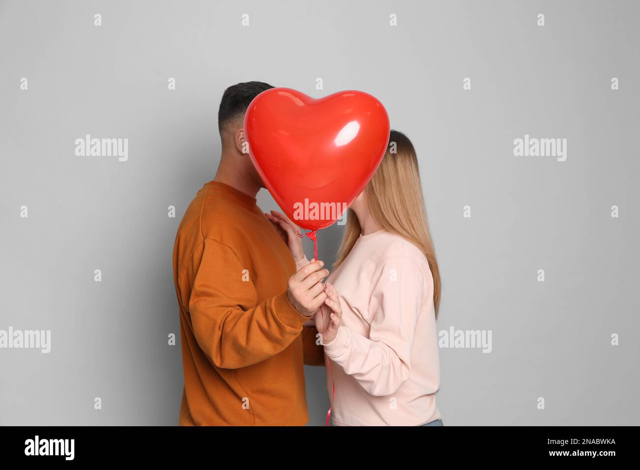 Lovely couple kissing behind heart shaped balloon on grey background ...