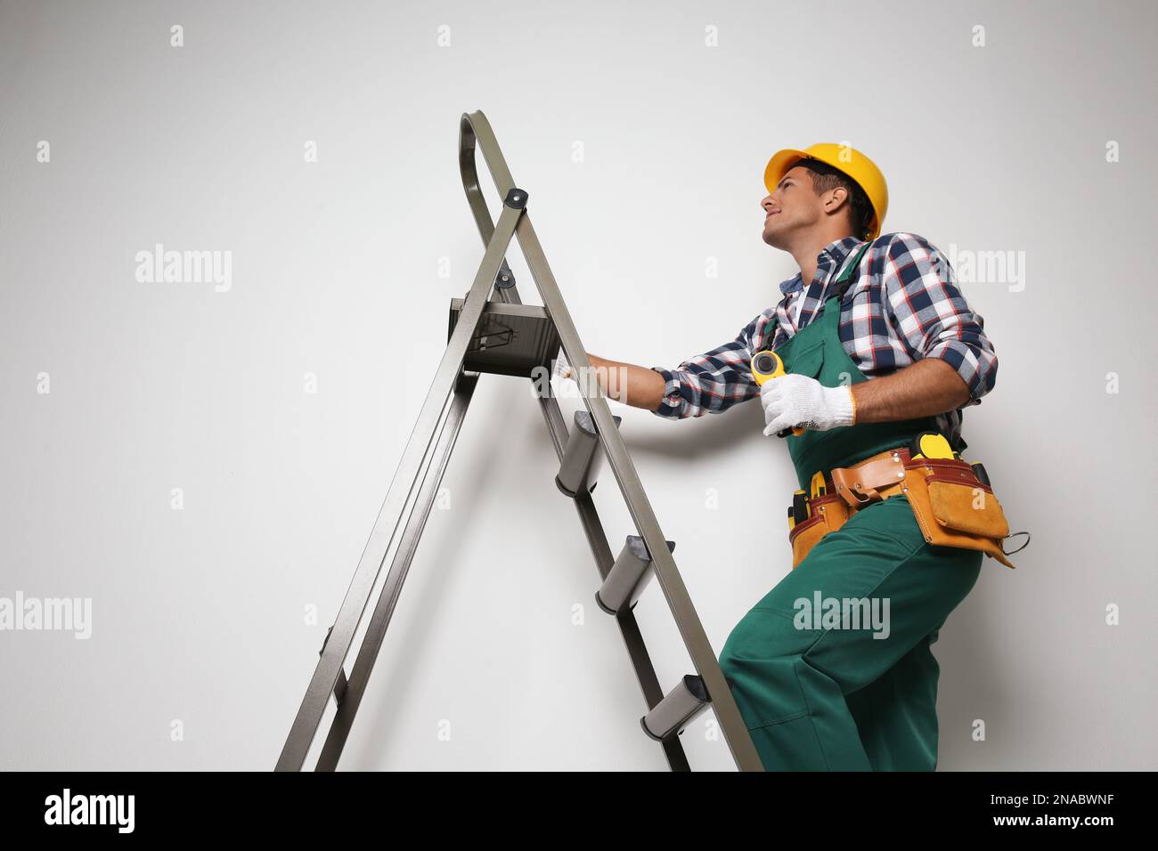 Professional builder climbing up metal ladder on light background Stock ...