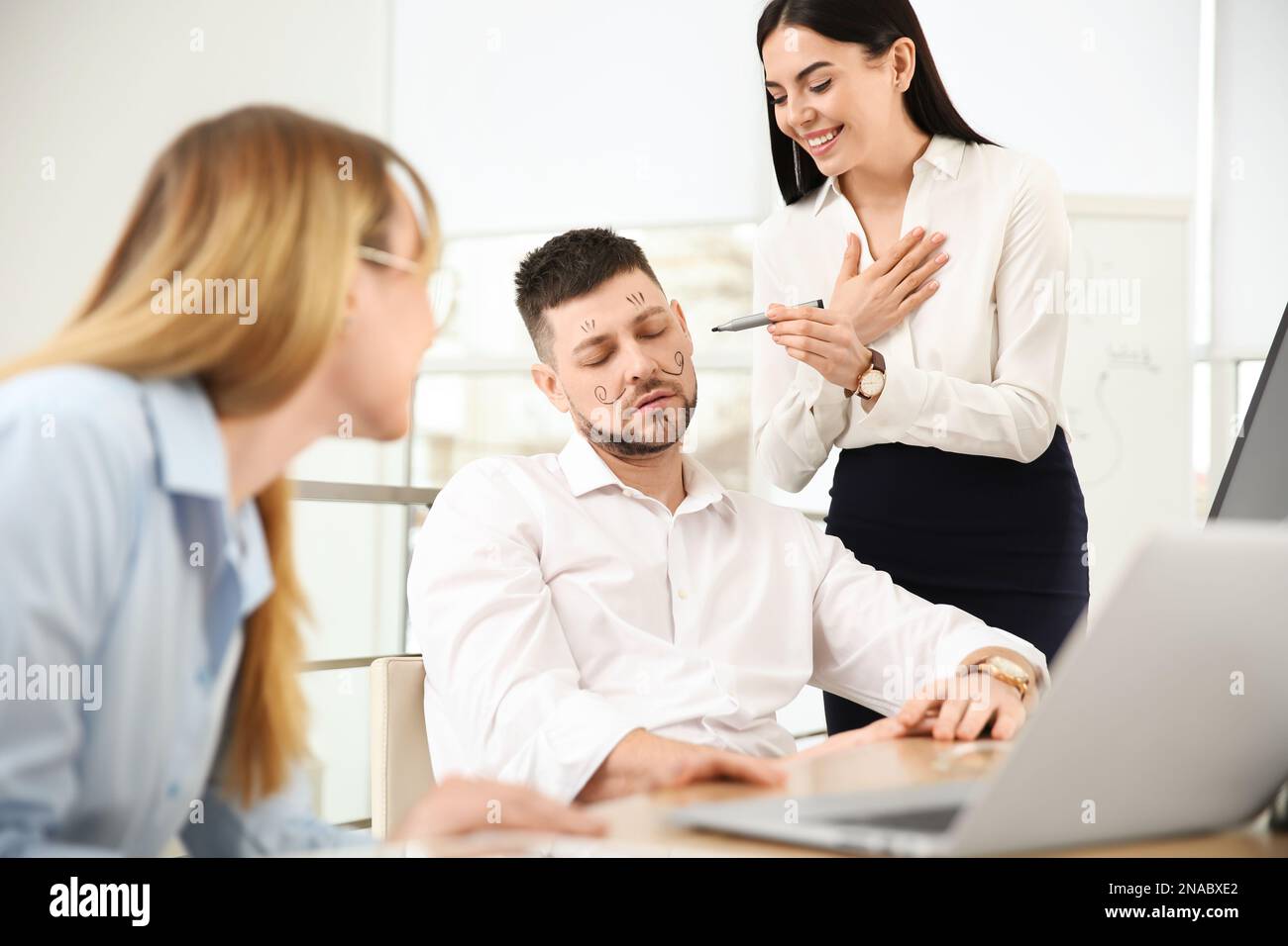 Young woman drawing on colleague's face while he sleeping in office ...