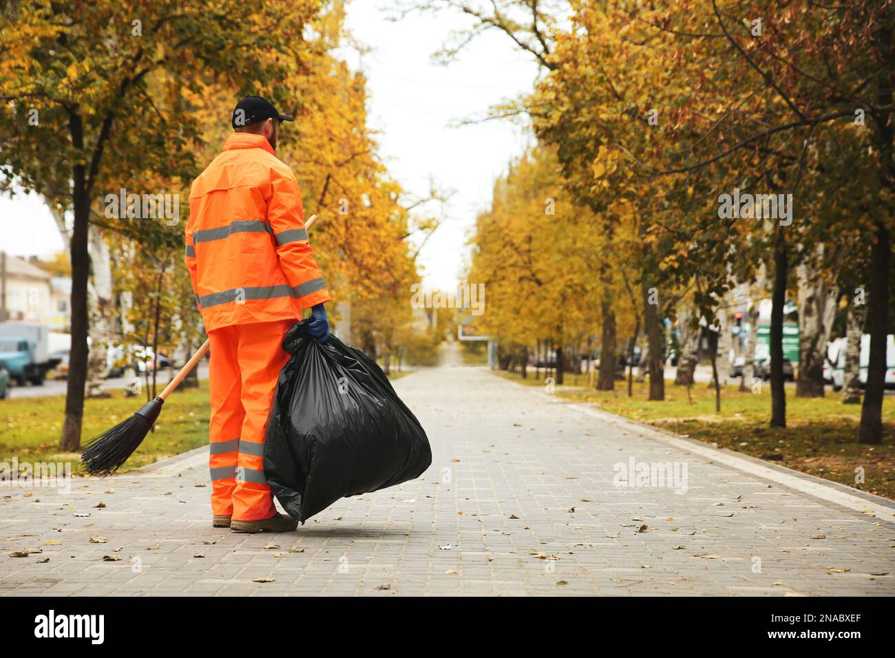 Street cleaner with broom and garbage bag outdoors on autumn day, back ...