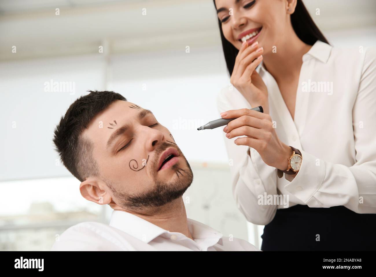 Young woman drawing on colleague's face while he sleeping in office ...