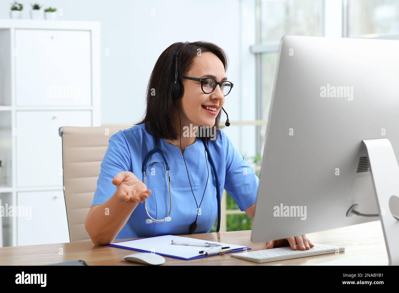 Doctor with headset and computer consulting patient online in office ...