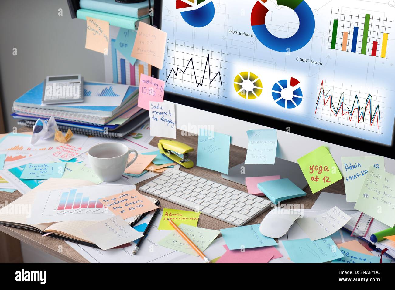 Computer, notes and office stationery in mess on desk. Overwhelmed with ...