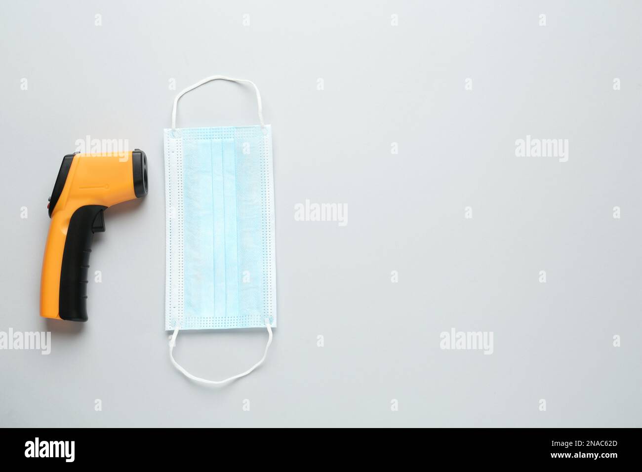 Infrared thermometer and medical mask on grey background, flat lay with ...