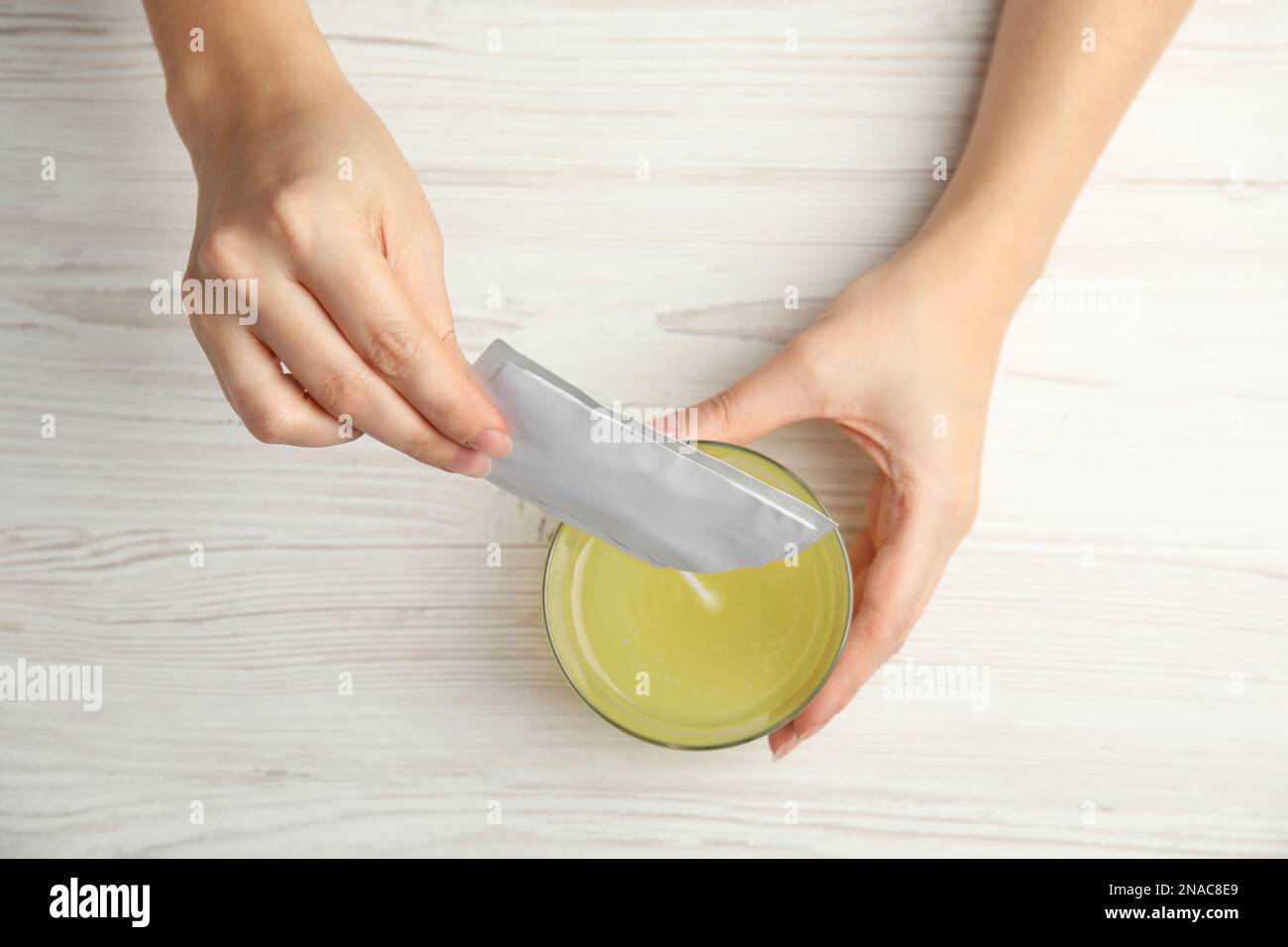 Woman pouring powder from medicine sachet into glass with water at ...