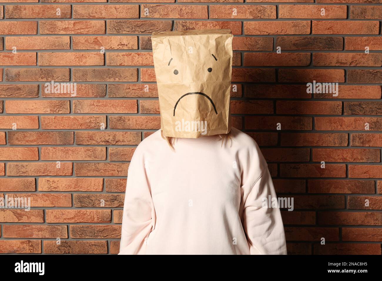 Woman wearing paper bag with drawn sad face near brick wall Stock Photo ...