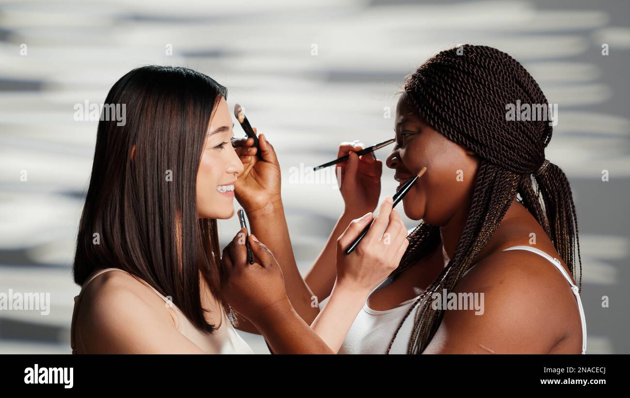 Diverse women playing with make up brushes in studio, giving eachother ...