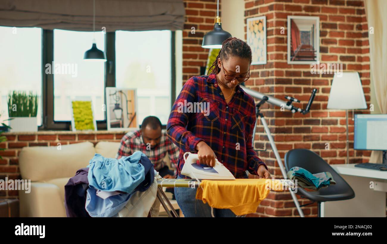 Young modern housewife using heat iron and ironing table, smoothing out ...