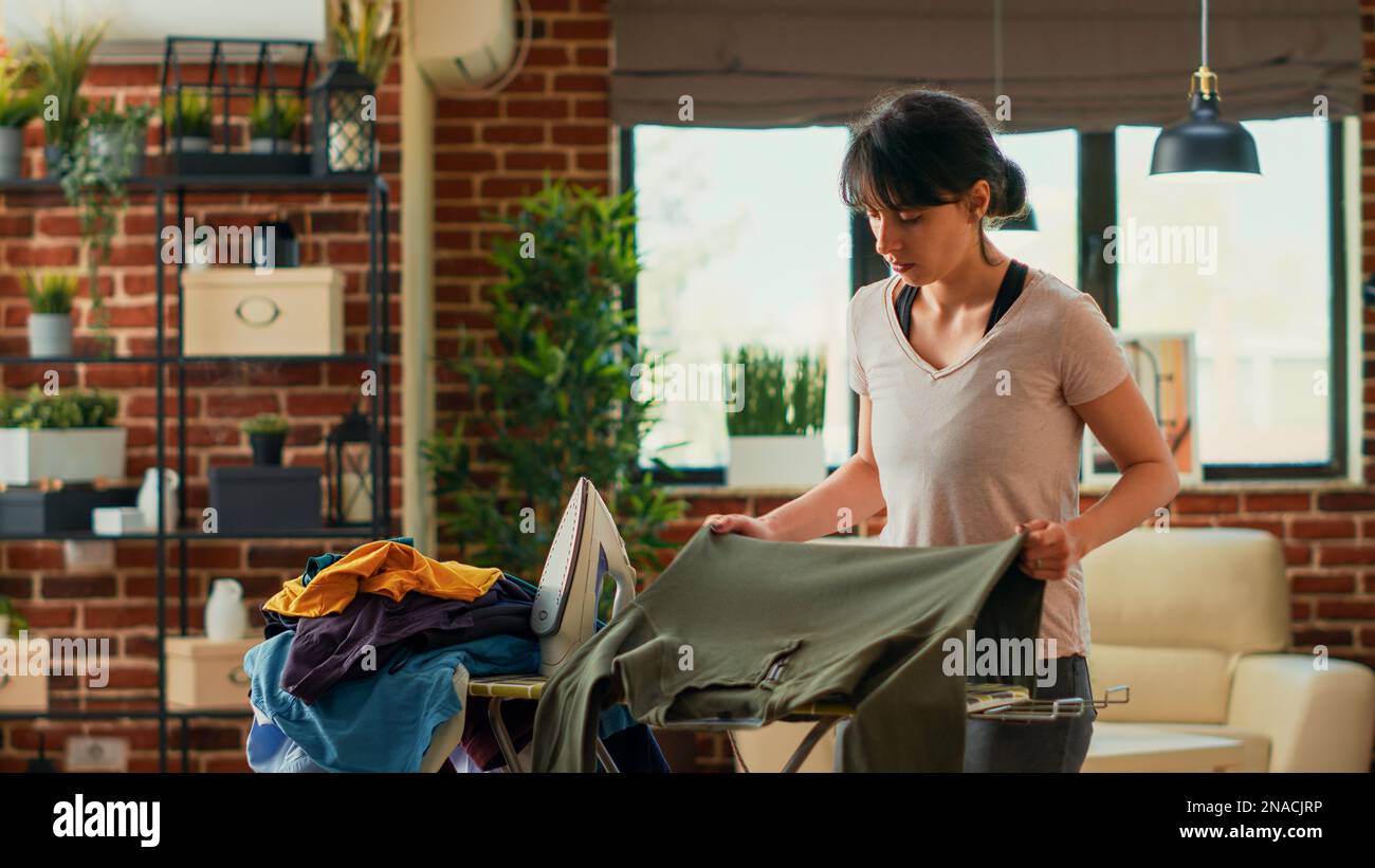 Young adult using steam iron to smooth out wrinkles on clothing ...