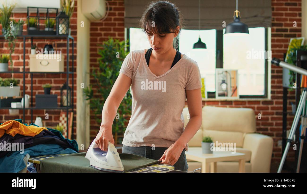 Modern woman ironing clothes at home after doing laundry, using heat ...