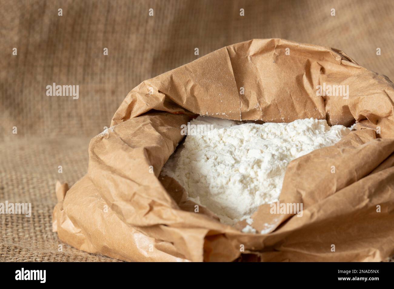 Plain white flour in a brown paper bag on hessian sack cloth. Eco ...