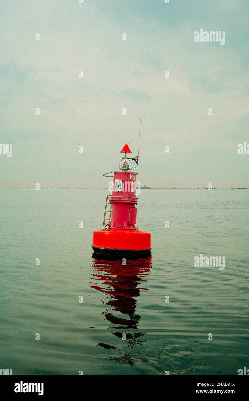 A vertical of a red beacon floating in the sea with the sky and the ...