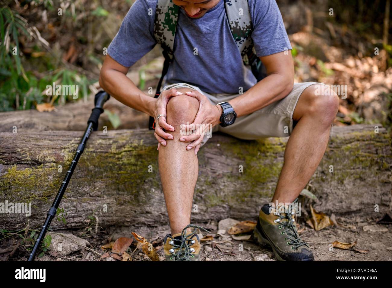 Cropped image of a stressed Asian male trekker sits on a wooden log and ...
