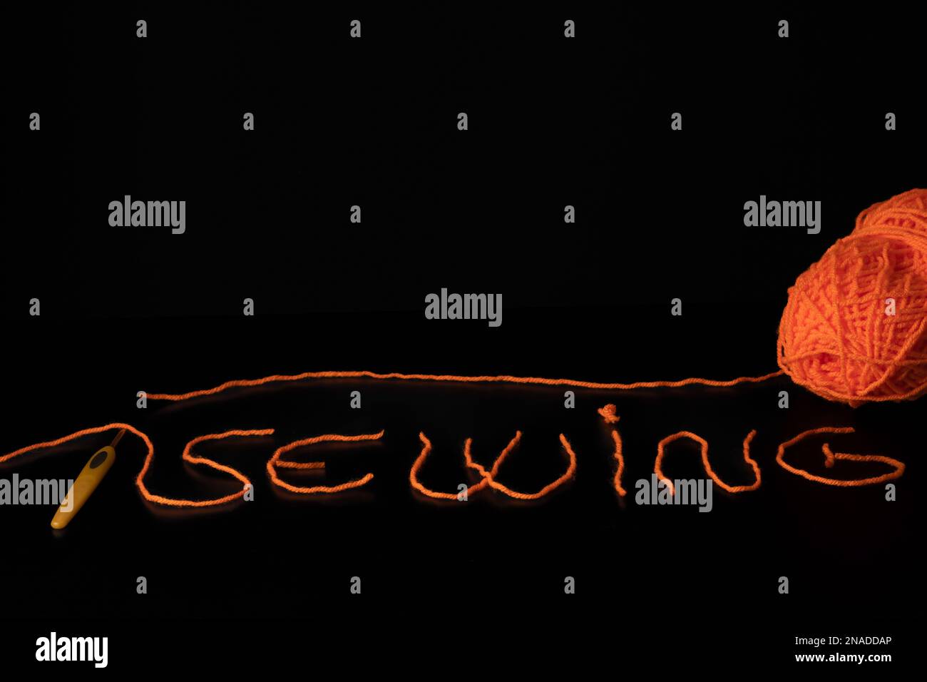 word sewing written with orange colored wool isolated on black ...