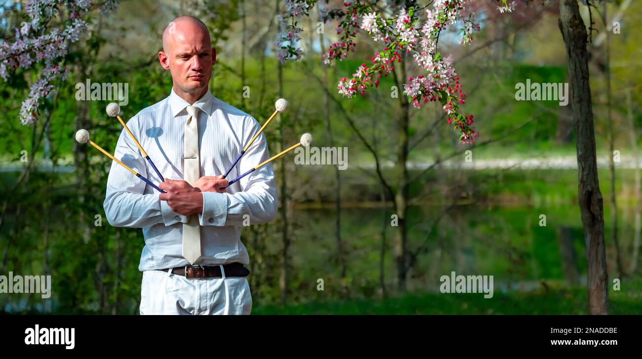 A shallow focus shot of a bald male holding four drum sticks and ...