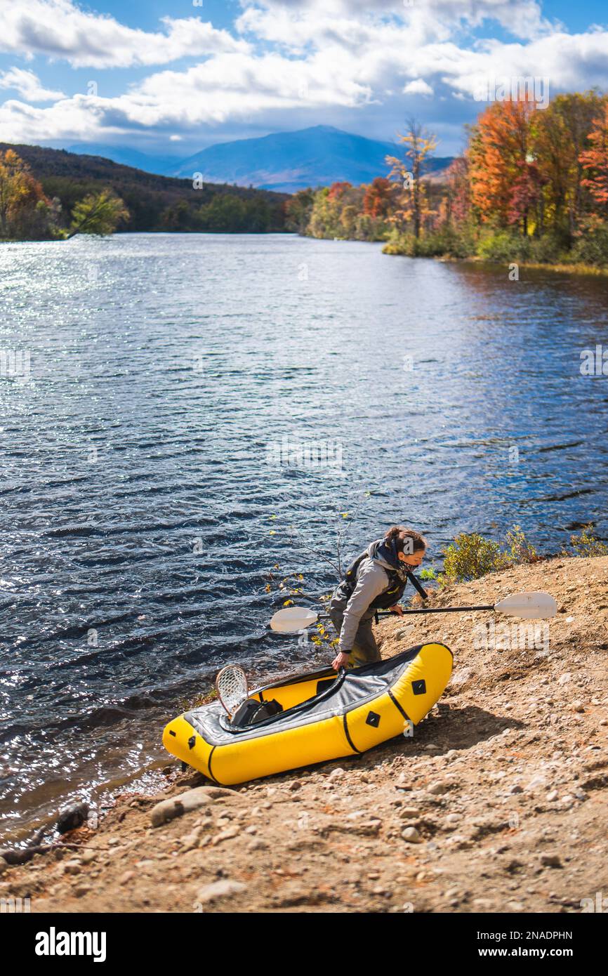 A woman angler pulling a pack-raft onto shore with a river behind Stock ...