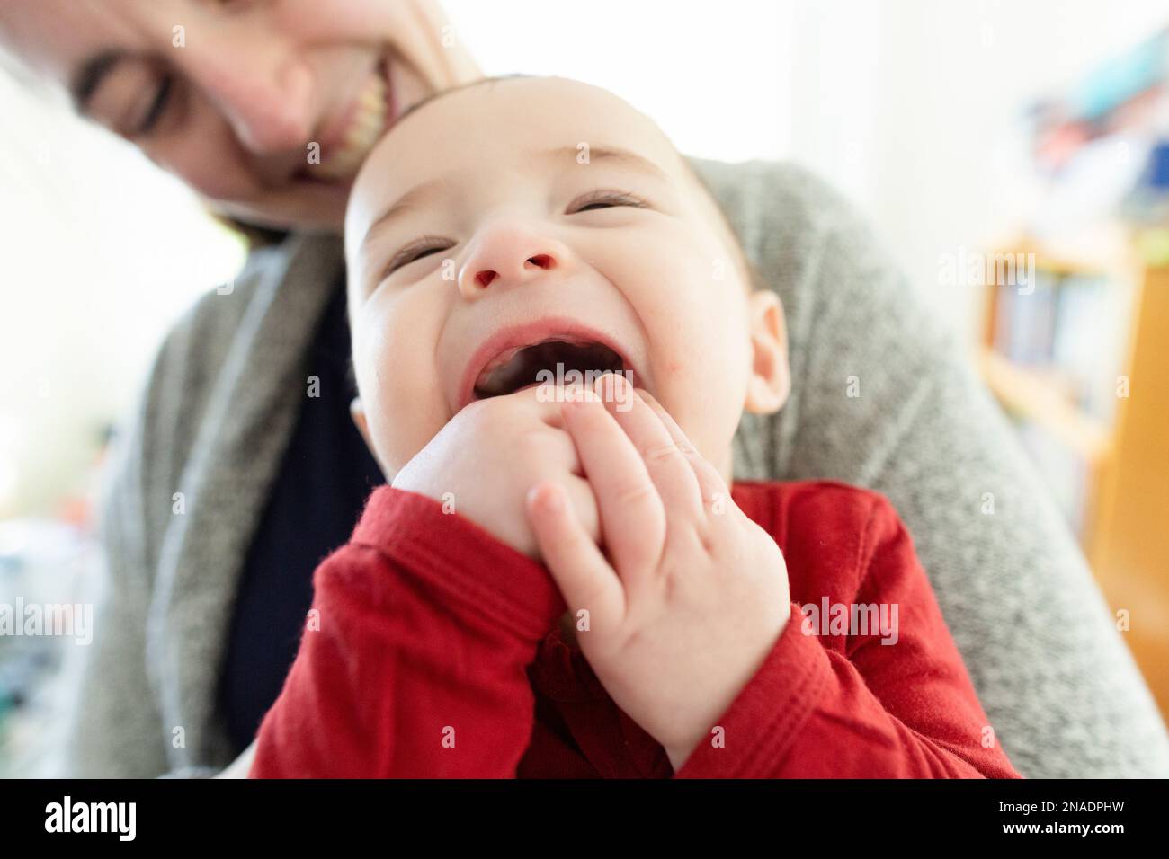 Baby Boy Smiling and Chewing on His Fingers While Being Held by Mom ...