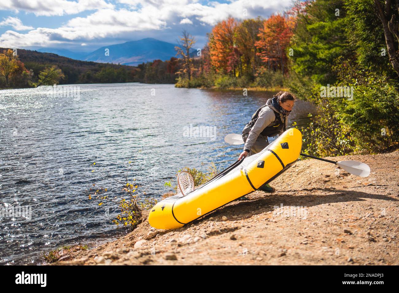 A woman angler pulling a pack-raft onto shore with a river behind Stock ...