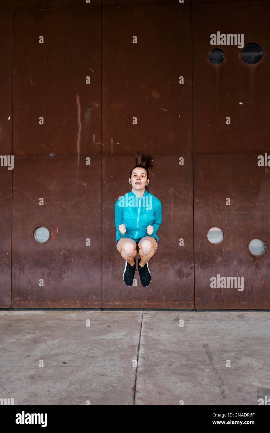 Side view of young runner woman jumping against wall on the stre Stock ...