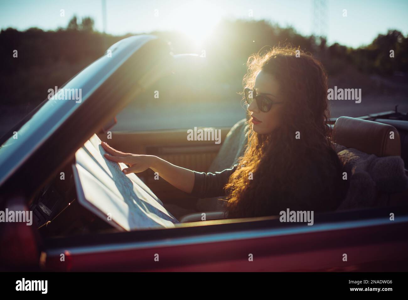 Woman with curly hair reading a map in the vintage car with suns Stock ...