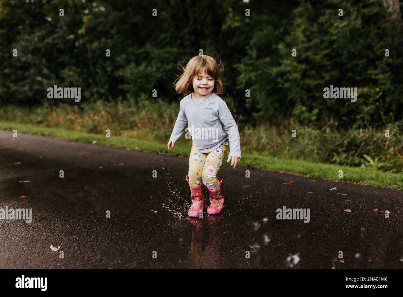 Young girl splashes in puddle on walking trail on a cloudy fall day ...