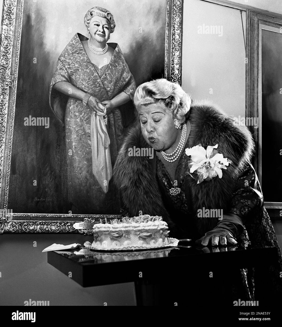 Singer Sophie Tucker blows out the candles on a birthday cake as she ...