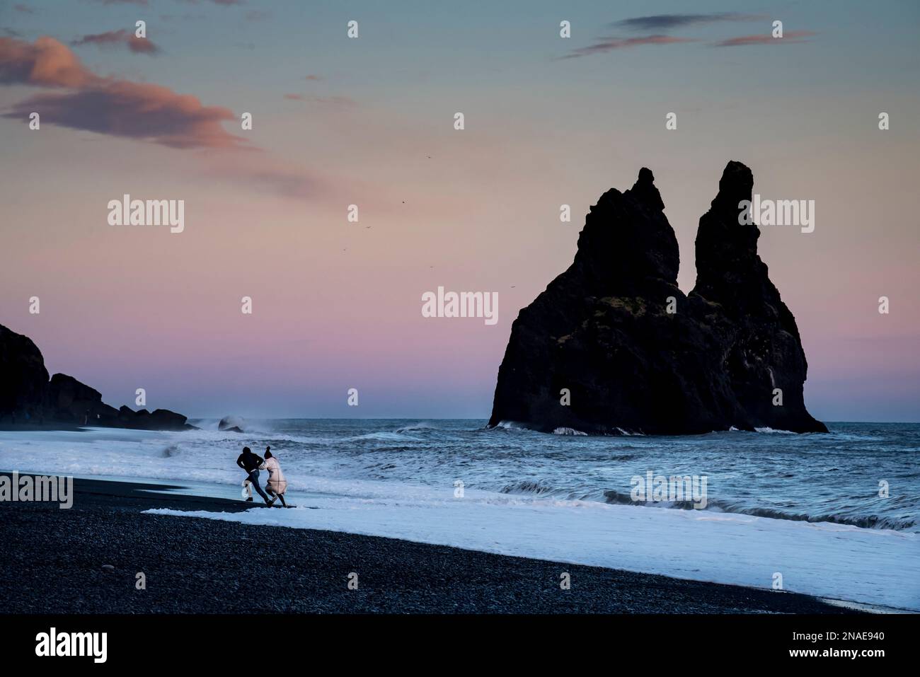 Tourist couple runs from the waves coming in to the beach with the tide ...