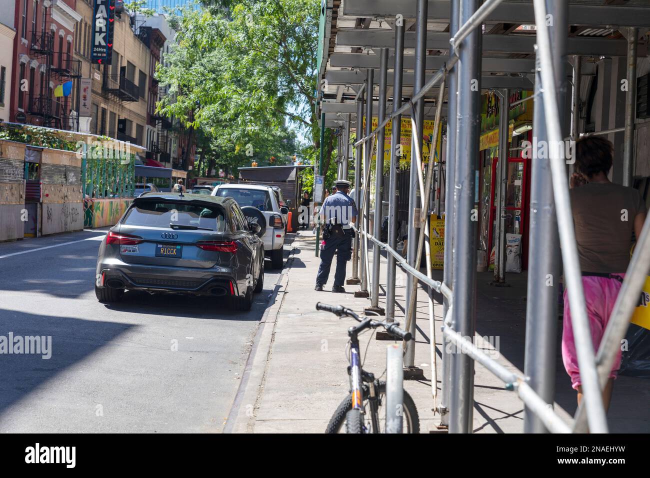 A busy street with many cars parked at the curb and a man walking in ...