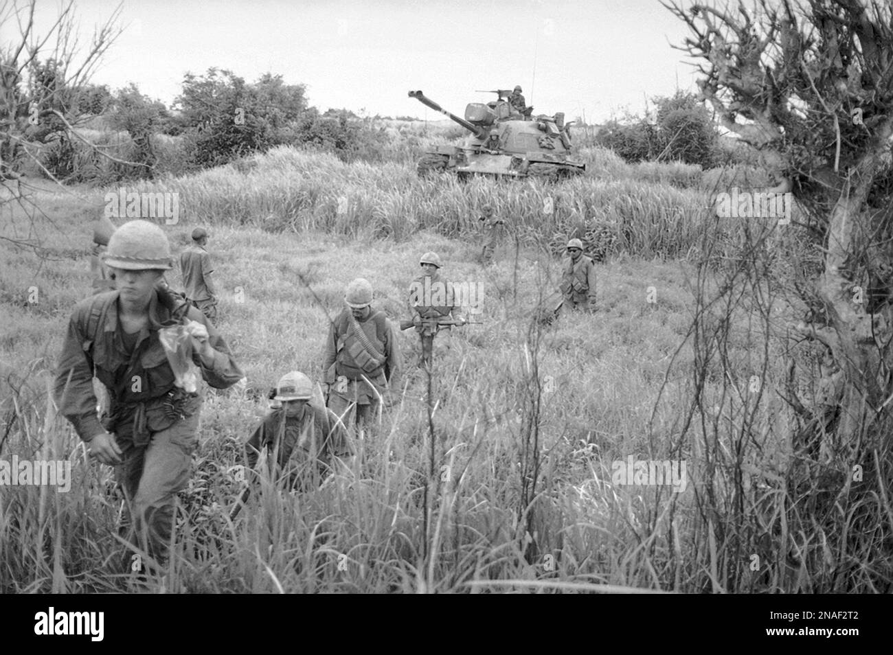 A tank hovers in the background as GIs walk single file through the ...