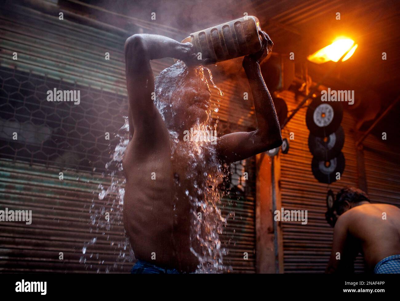An Indian man bathes as he pours cold water over his head in a market ...