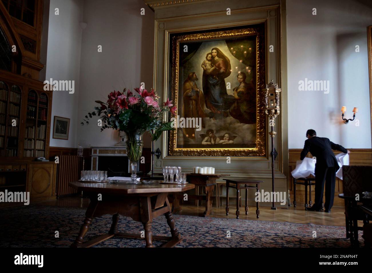 Waiter unfolds linen table cloths as he prepares a dining room for the ...