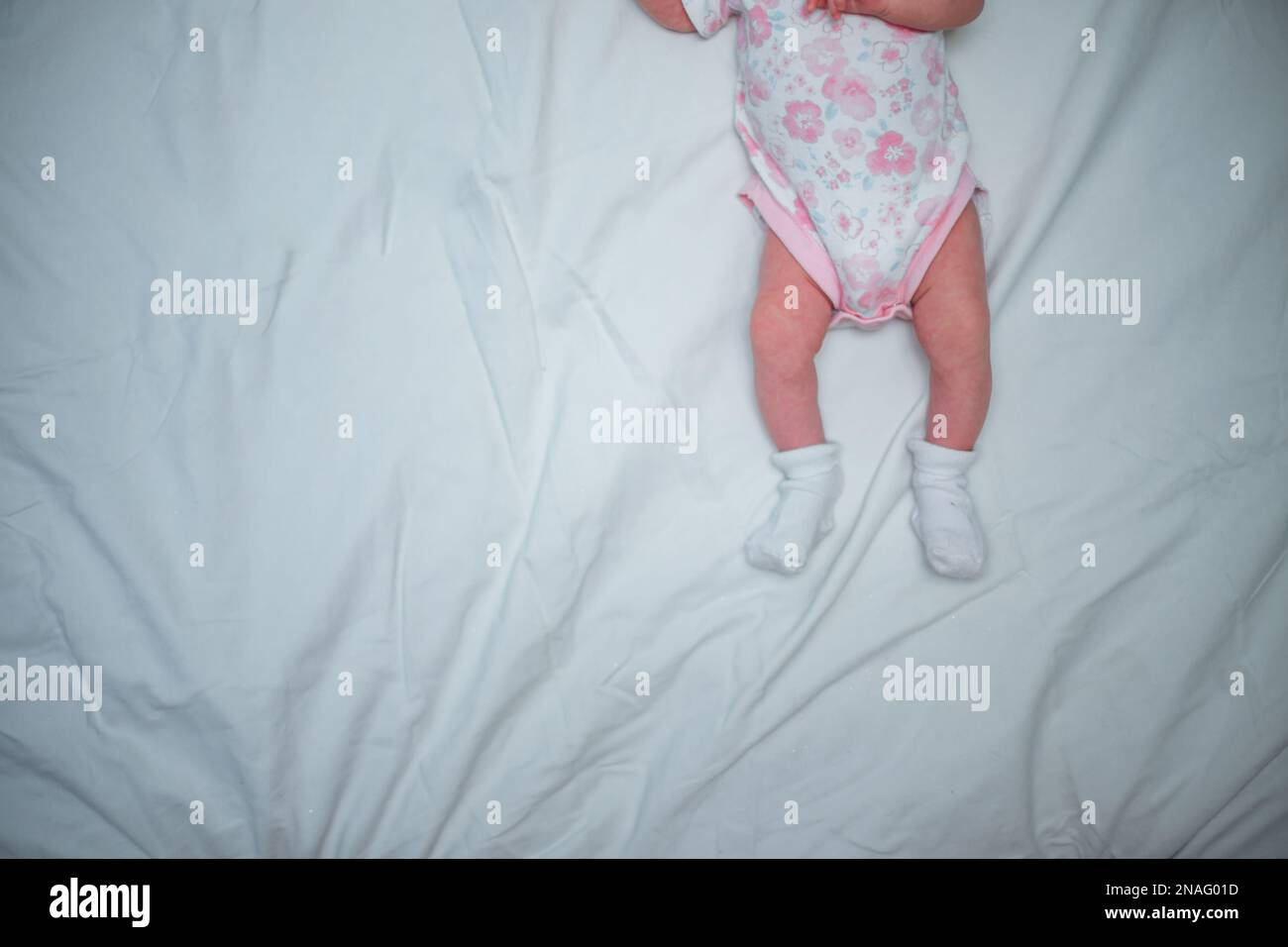baby on bed. Newborn baby in white bodie. Legs of tiny newborn in white ...