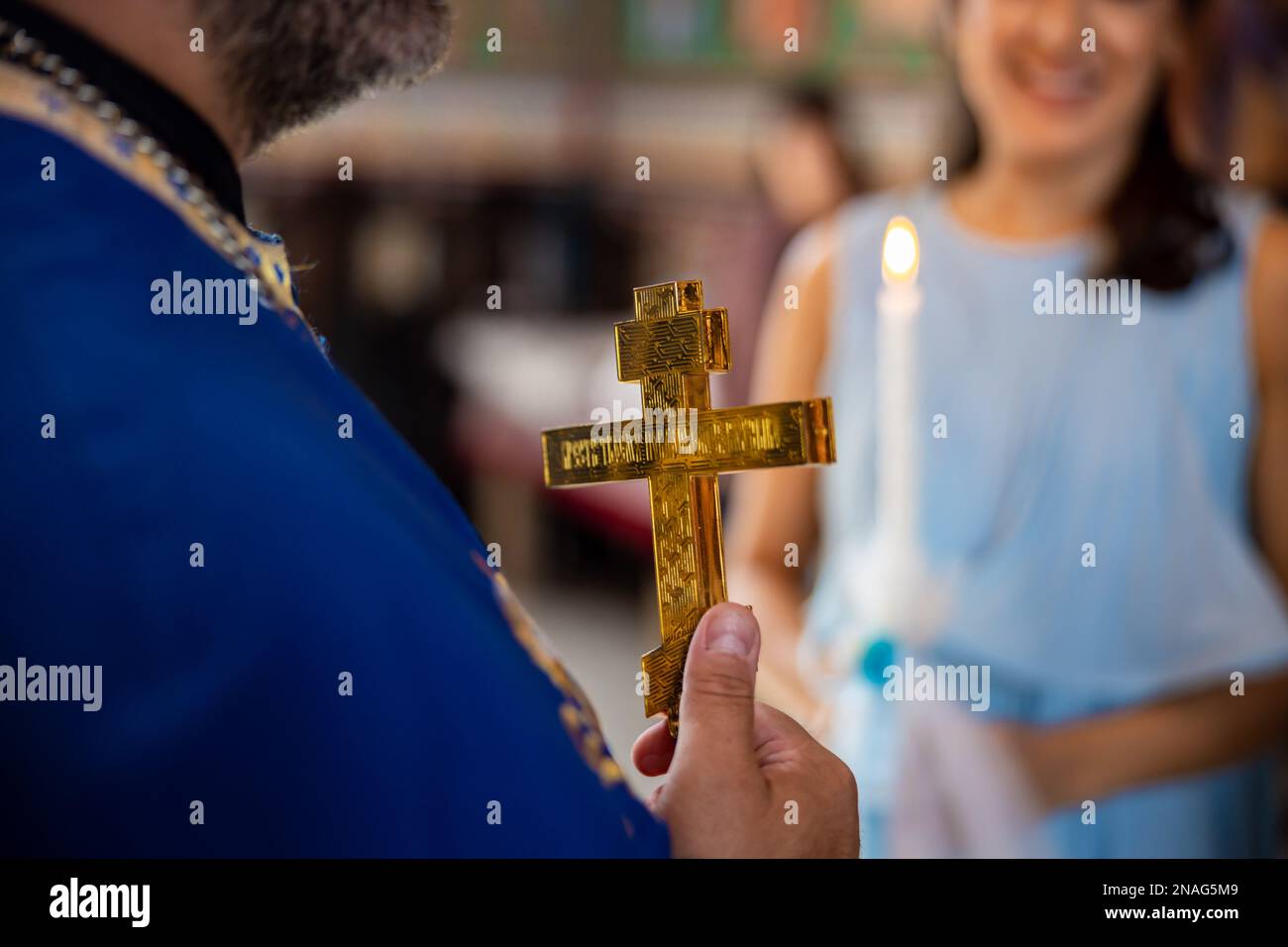 A priest holding a golden cross in front of the family mother. Children ...