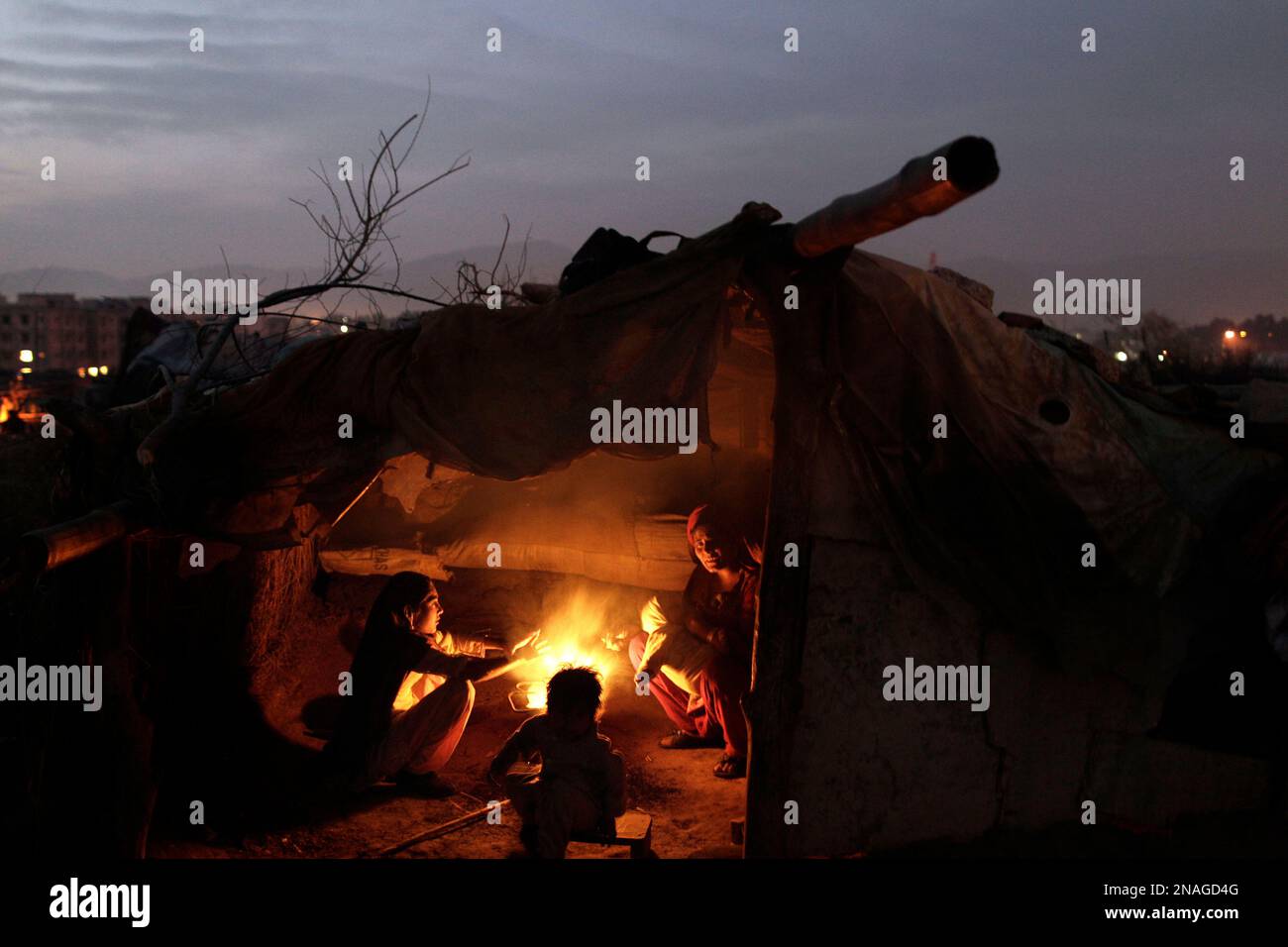 A Pakistani family gather a round a fire inside a shanty, to warm ...