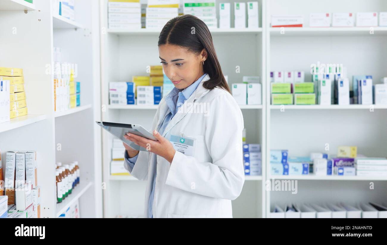 A young female pharmacist stocktaking in a dispensary using a tablet ...