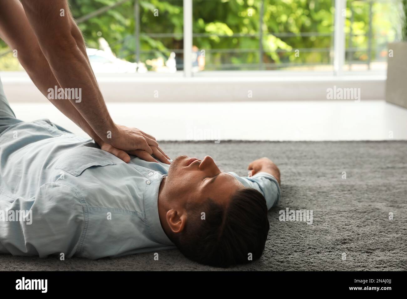 Passerby performing CPR on unconscious man indoors. First aid Stock ...