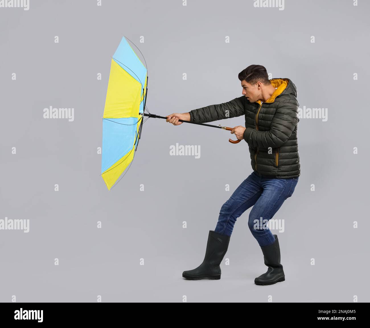 Emotional man with umbrella caught in gust of wind on grey background ...