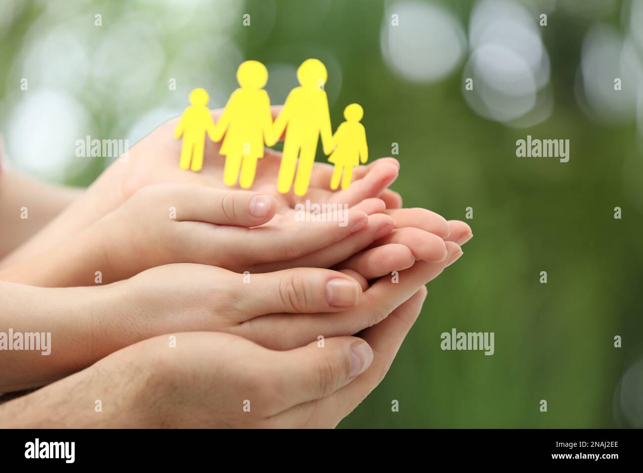 Parents and kid holding paper cutout of family in hands outdoors ...