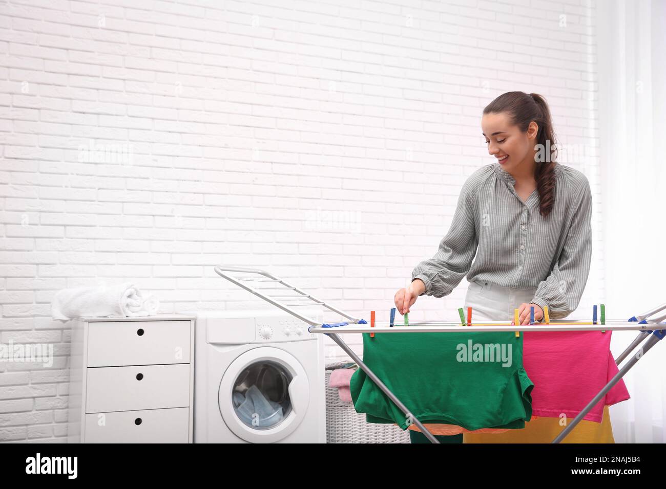 Young woman hanging clean laundry on drying rack indoors Stock Photo ...