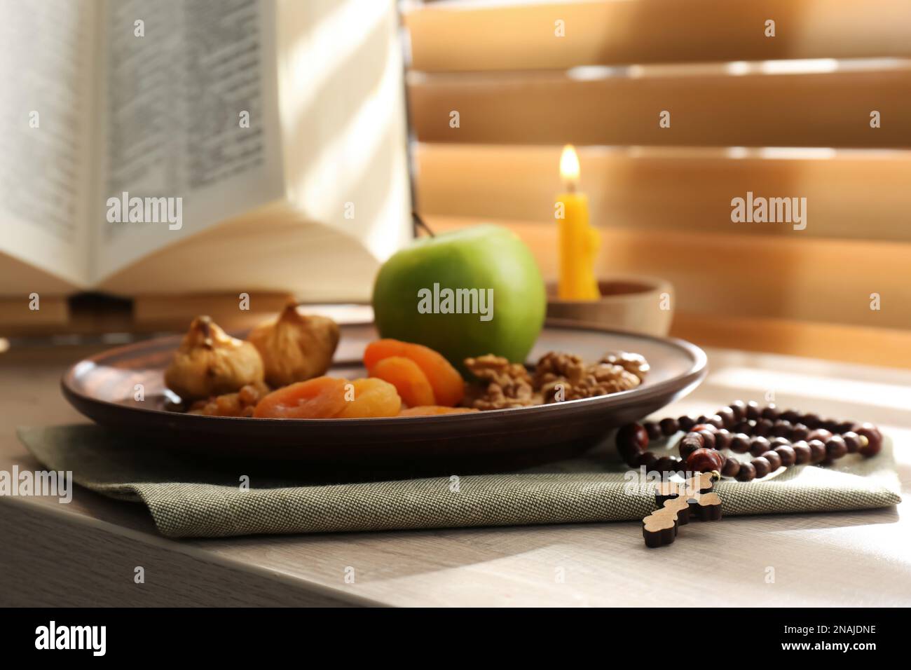 Dried fruits, apple, prayer beads, Bible and candle on window sill ...