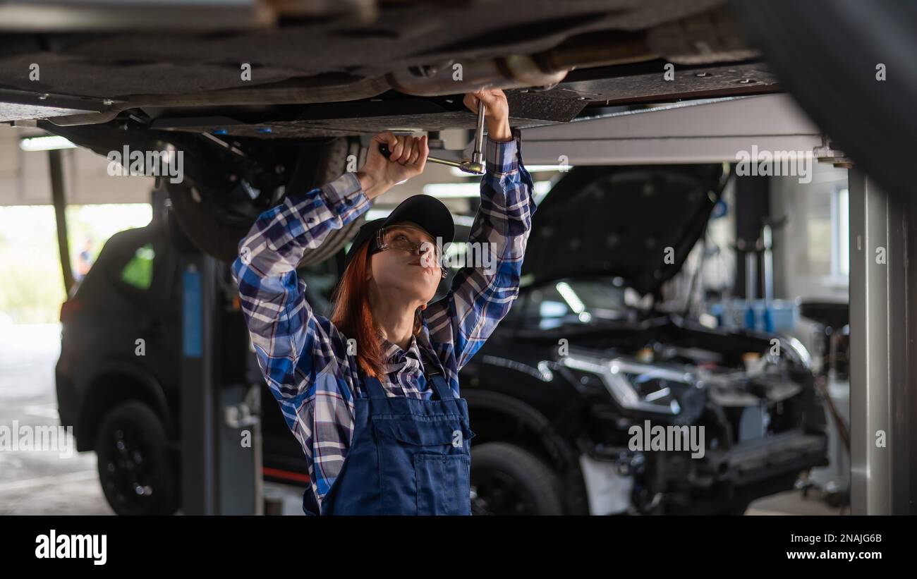 Female mechanic unscrew the nuts on the bottom of the car that is on ...