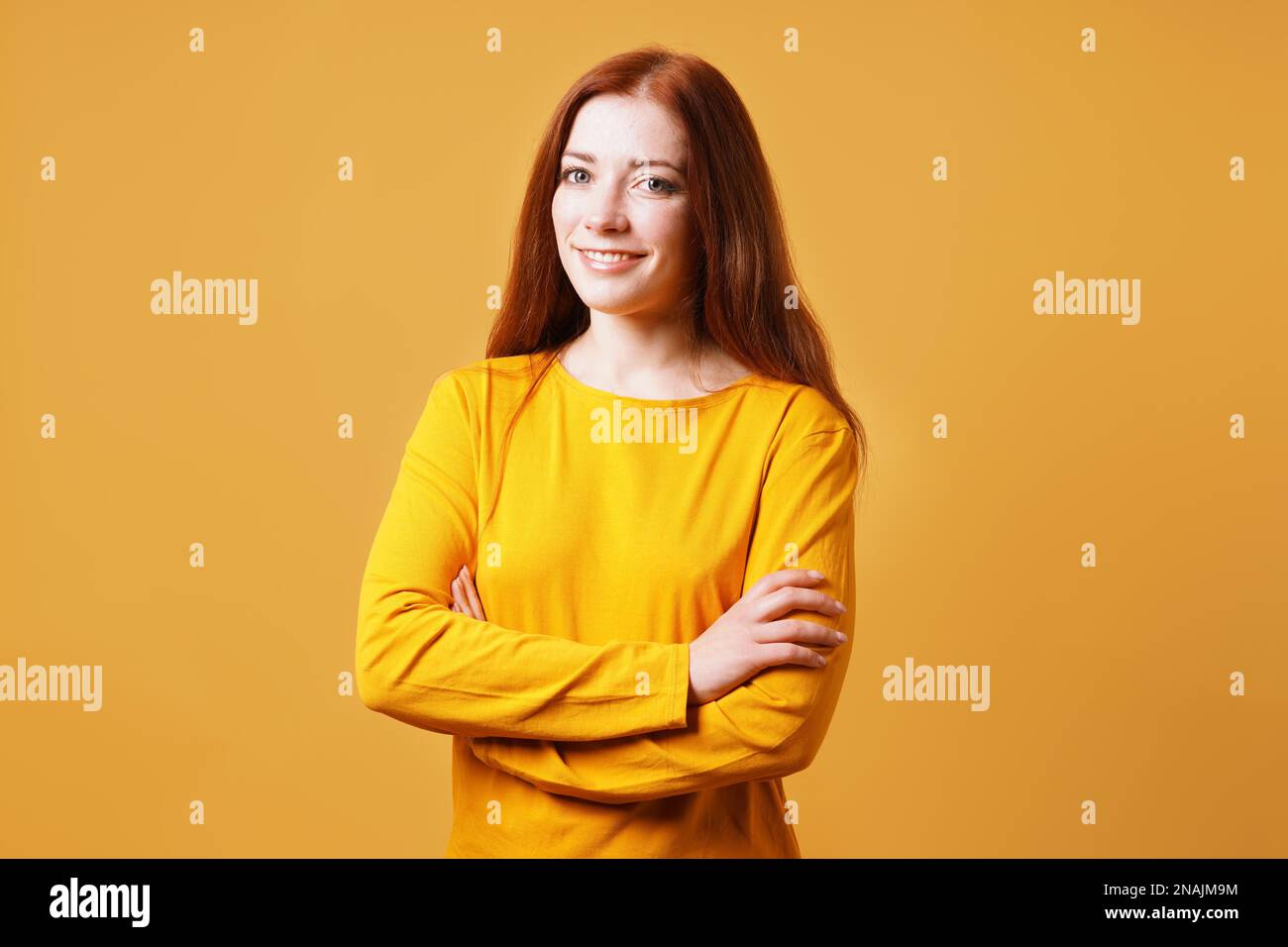 happy confident young woman with her arms folded smiling into camera ...
