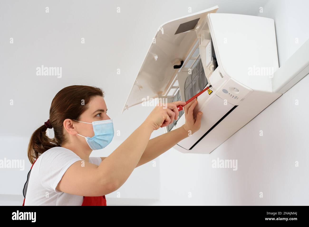 Female technician wearing face mask and repairing air conditioner ...