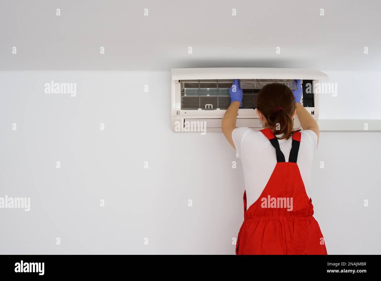 Female technician wearing face mask and cleaning air conditioner ...