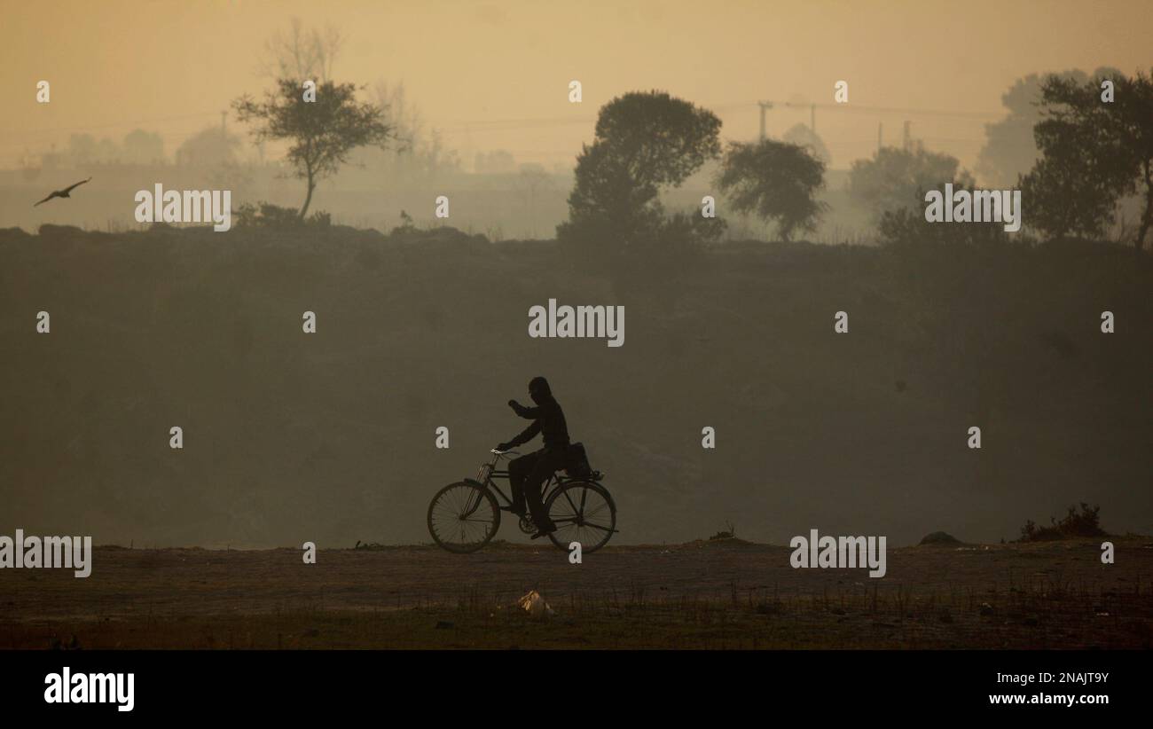 A Pakistani man rides his bicycle along a dusty road during the sunrise ...
