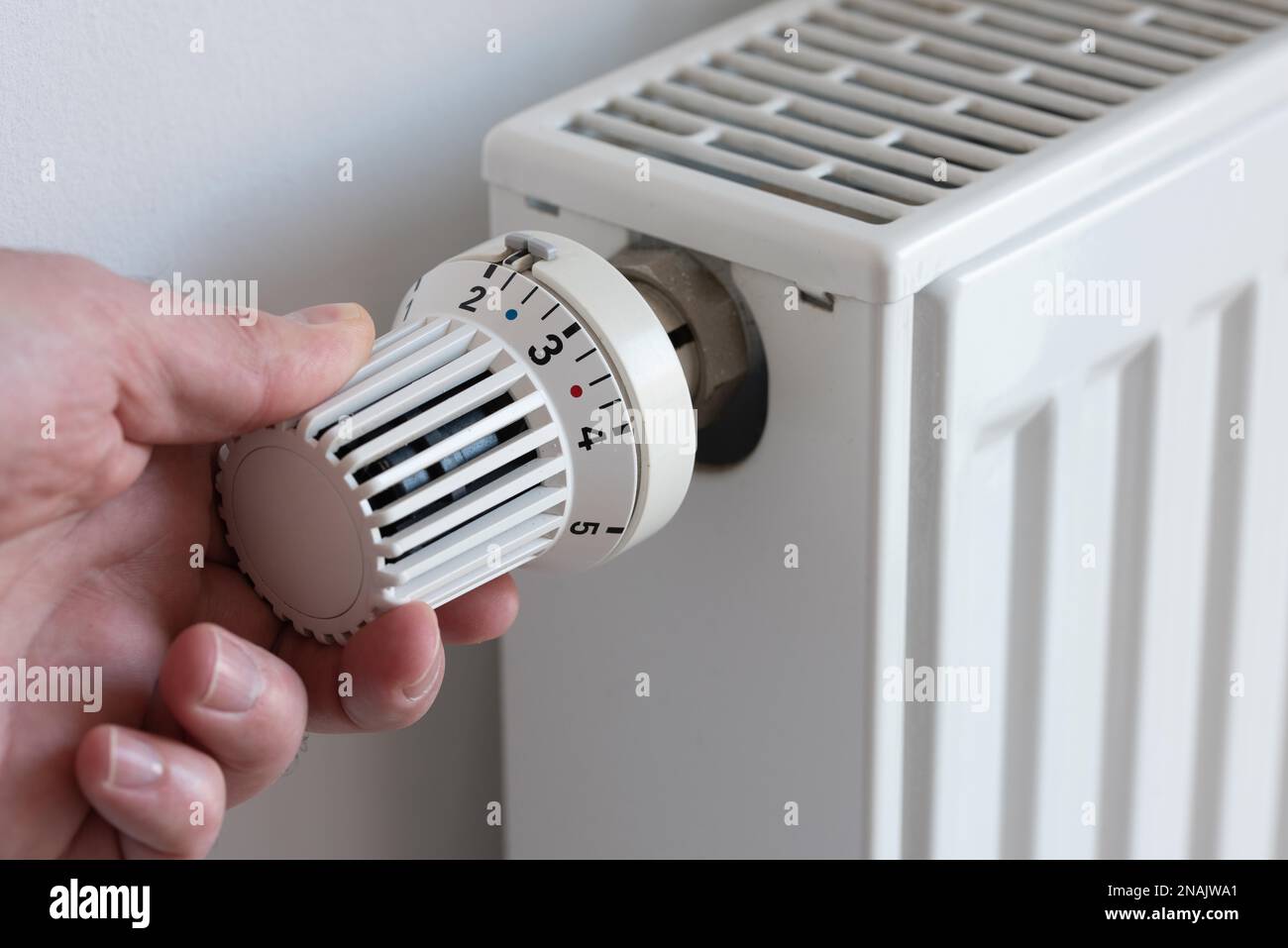 close-up of person turning down thermostat on heater to save energy ...