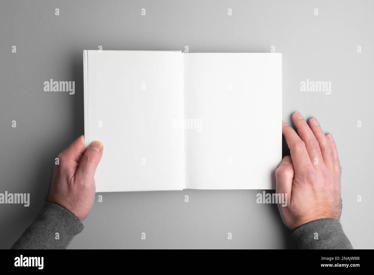 overhead view of person opening blank page hardcover book on gray desk ...