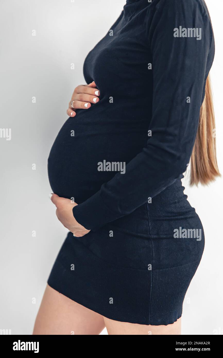 A pregnant woman in a black short dress on a white background, belly ...